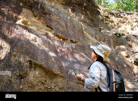 Female Geologist With Backpack Exploring Nature Trail In Forest And Analyzing Rock Or Gravel
