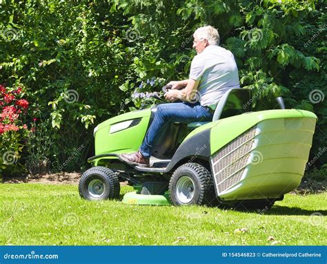 Senior Man Driving A Tractor Lawn Mower In Garden With Flowers Stock