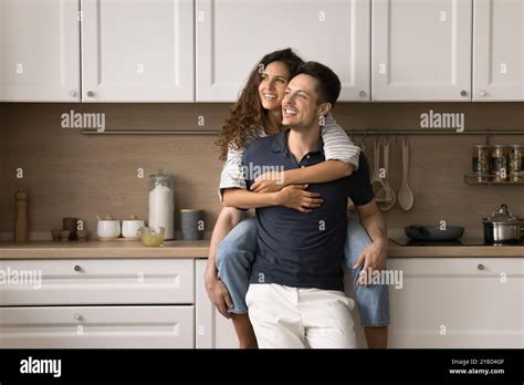 Happy Dreamy Wife Sitting On Kitchen Counter Embracing Husband Stock