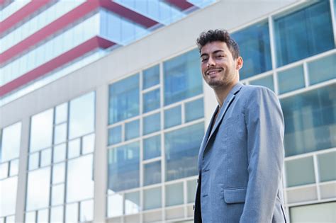 정장을 입은 백인이자 자신감 넘치는 젊은 남성이 외부 건물 사무실 앞에서 미소를 지으며 카메라를 바라보는 모습의 미디엄 샷 25 29세에 대한 스톡 사진 및 기타 이미지