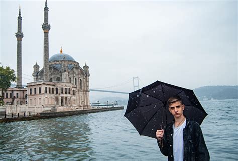 비오는 날에 1518 세의 잘 생긴 젊은 십대 남자가 비에 서서 우산을 들고 카메라를 봅니다 내추럴 블루 바다 배경 선택적 초점