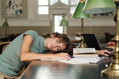 Young Tired Female Student Sleeping On Desk With Books Around During