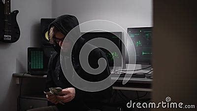 A Hacker In The Computer Room A Man In A Jacket With A Hood Glasses And Money In Hands Sitting
