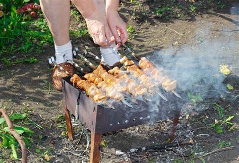 A Woman Turns The Meat On Skewers Which Is Cooked On The Grill A
