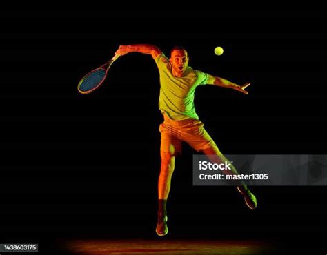 네온 불빛의 어두운 배경 위에 고립된 테니스를 하는 스포츠웨어를 입은 활기찬 남성 테니스 선수의 역동적인 초상화 모션 속도 프로 스포츠의 개념 네온에 대한 스톡 사진 및