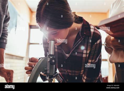 School Girl In Science Class Using A Microscope With Teacher And