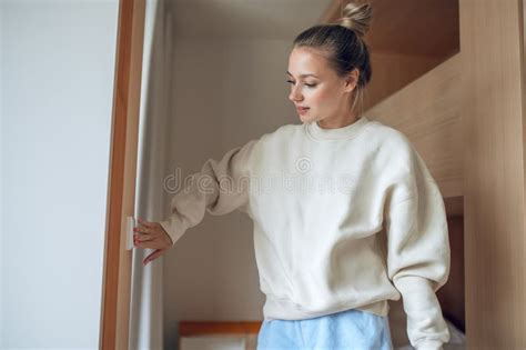 Girl In White Standing Near The Window And Fixing The Curtain Stock