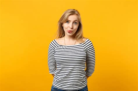 스튜디오에서 노란 오렌지 벽 배경에 고립 된 혀를 보여주는 카메라를 찾고 줄무늬 옷에 재미 젊은 여자의 초상화 사람들은 진심으로 감정 라이프 스타일 개념입니다 복사 공간을