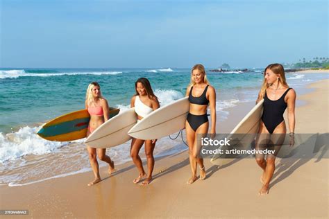 네 명의 젊은 여성이 서핑 보드를 들고 햇볕이 잘 드는 해변을 걷고 있습니다 친구들은 수영복을 입고 해변에서 하루를 즐깁니다 파도가 부서집니다 서핑 모험 해안 라이프스타일