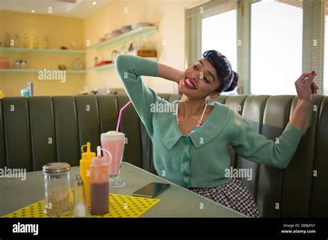 Smiling Woman Stretching Arms Behind Head At Diner Booth With Milkshake And Smartphone Copy