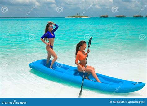 Two Bikini Models In Swimwear Posing On Kayak On Tropical Beach