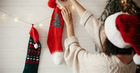 아늑한 스웨터를 입고 산타 모자를 쓴 세련된 소녀는 흰 벽에 스타킹 화환 조명 크리스마스 트리가 있는 크리스마스 휴일을 장식하고 있습니다 즐거운 성탄절 즐거운 휴일