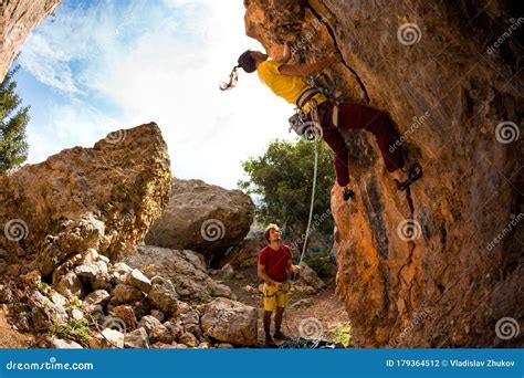 The Girl Climbs The Rock In The Shape Of An Arch A Man Is Belaying A