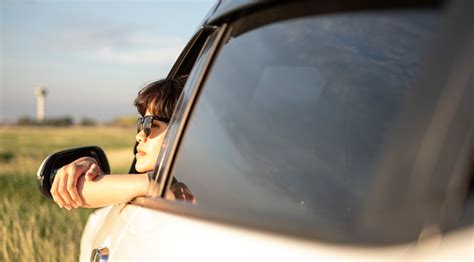 짧은 머리를 가진 아시아 관광 여성은 차 안에 앉아있는 선글라스를 착용하고 차에서 튀어 나와 편안하고 차분하고 행복한 분위기로 여름철 도로 여행에서 자연을 바라 봅니다 바람