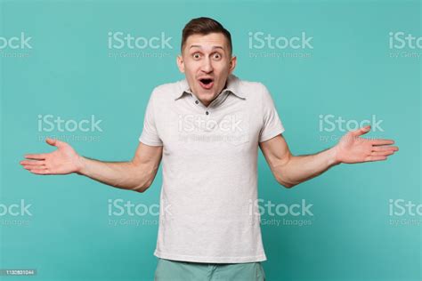 입을 열어 유지 캐주얼 의류에 깜짝 젊은 남자 스튜디오에서 파란색 청록색 벽 배경에 고립 된 손을 확산 사람들은 진심으로 감정