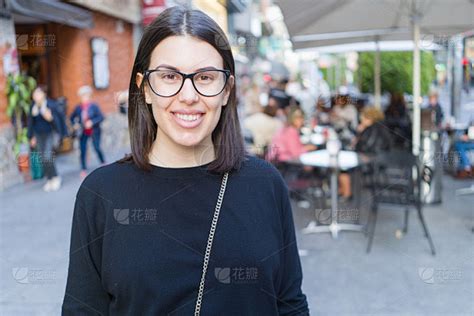 美丽年轻的黑发女人微笑着兴奋地走在城市的街道上，快乐和自信的表情站在城镇的户外