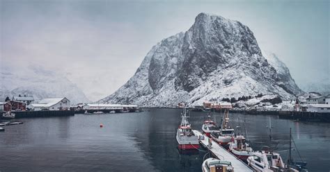 노르웨이 로포텐 제도의 함노이 어촌 마을에 배가 있는 부두에는 빨간 로르부 집이 있습니다 내리는 눈과 함께 사진 Unsplash의 피오르 이미지