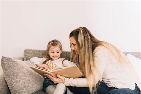 Веселая мать читает книгу дочери возле дивана Бесплатно Фото