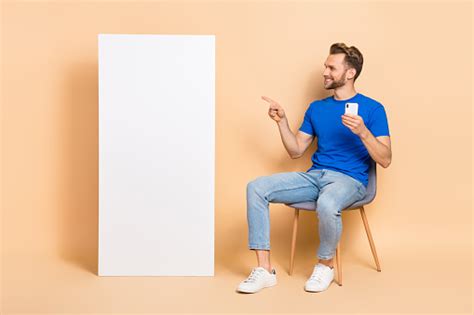 잘 생긴 남자의 전체 크기 초상화는 의자 모양 직접 손가락 빈 공간 디스플레이 베이지 색 배경에 고립 되어 있습니다 25 29