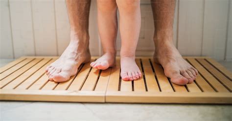 알아볼 수 없는 아버지와 집에 있는 욕실의 나무 목욕 매트에 서 있는 유아의 다리 육아 휴직 사진 Unsplash의