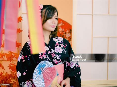 둥근 종이 팬을 손에 들고 미 닫이 문 앞에 서 서 누군가 기다리고 전통적인 일본 기모노를 입고 매력적인 아시아 여자의 초상화