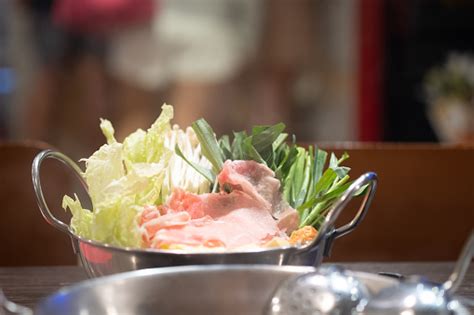돼지 고기 쇠고기 신선한 야채의 인기 요리인 샤브 샤브 또는 스키야키 일식 레스토랑에서 끓는 냄비가있는 테이블에 놓습니다 0명에