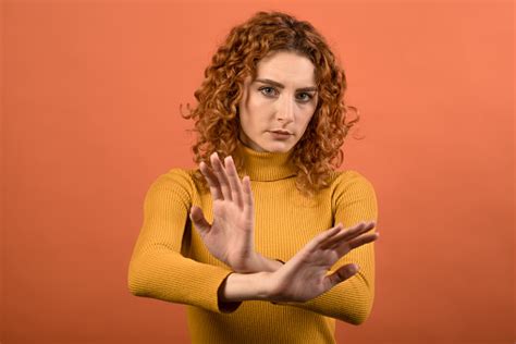 오렌지 스튜디오 배경에 고립 된 부정적인 제스처를 보여주는 교차 팔을 가진 오렌지 점퍼를 입은 젊고 매력적인 빨간 머리 백인 소녀 심각한에 대한 스톡 사진 및 기타 이미지