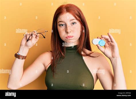 Young Red Head Girl Holding Glasses And Contact Lenses Puffing Cheeks