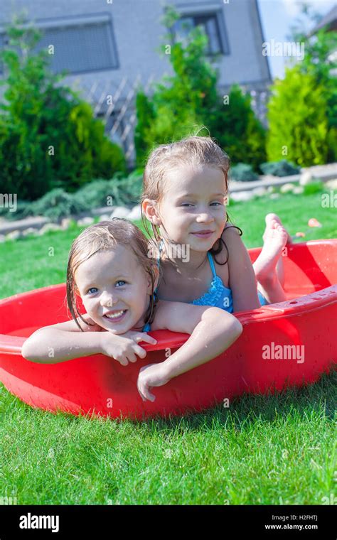 Two Little Sisters Playing And Splashing In The Pool On A Hot Sunny Day