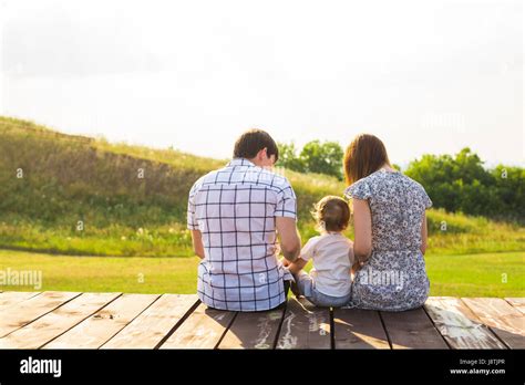 Rear View Of Mother Father And Son Sitting Together Outdoors Stock