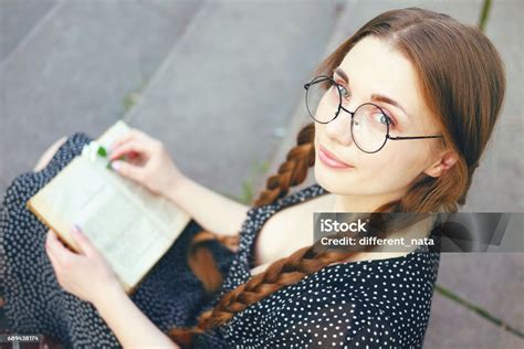 젊은 학생 여자 가방 및 철도 또는 버스 역에서 기다리고 긴 머리 띠와 하얀 점 들과 검은 드레스를 착용 하는 안경 레트로 패션입니다 땋은 머리에 대한 스톡 사진 및 기타