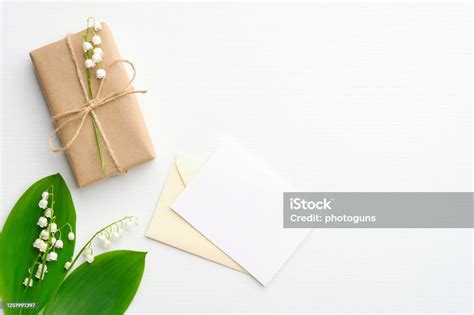 크래프트 페이퍼로 싸인 선물 또는 선물 상자 계곡의 꽃 백합 흰색 테이블에 빈 종이 카드가있는 낭만적 인 편지 플랫 레이 상단