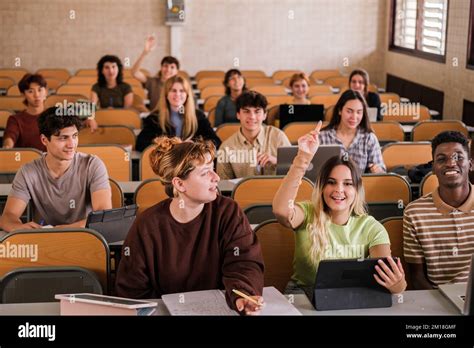 Group Of College Students Raising Their Hands To Ask The Teacher During Group Of College Students Raising Their Hands To Ask The Teacher During