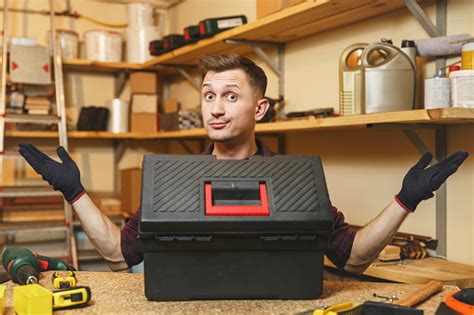 잘생긴 놀된 카리스마 백인 젊은이 격자 무늬 셔츠 검은 티셔츠 장갑 손 나무 테이블에서 목공 워크숍에서 작업을 확산 검은 도구 상자 및 다른 도구와 장소 T 셔츠에 대한