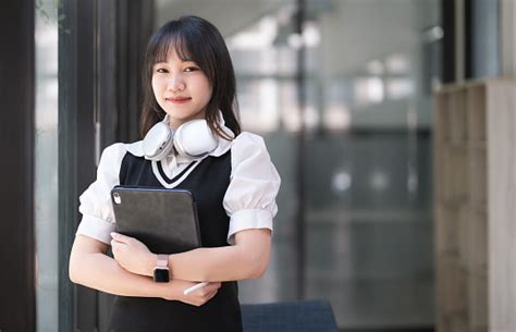 예쁜 젊은 여대생이 도서관에 서서 디지털 태블릿을 손에 들고 카메라를 향해 웃고 있다 25 29세에 대한 스톡 사진 및 기타