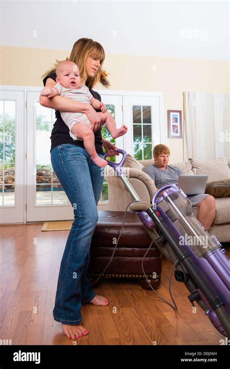 Mother With Son Using Vacuum Cleaner While Father In Background Stock
