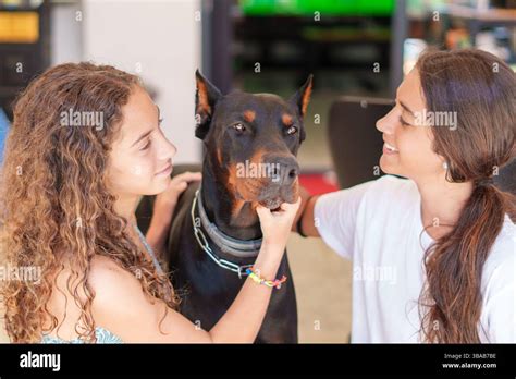 Two Teenage Girls Playing With Their Doberman Breed Dog In The Backyard