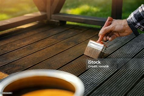페인트 브러시로 데크 보드에 갈색 나무 보호 오일을 바르는 사람 테라스 리노베이션 그림 그리기에 대한 스톡 사진 및 기타 이미지