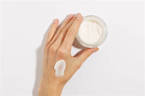 크림을 바른 여자의 손은 하얗고 고립된 배경에 얼굴 보습제가 든 흰색 유리병을 들고 있습니다 미용 스킨 케어 및 영양 제품의