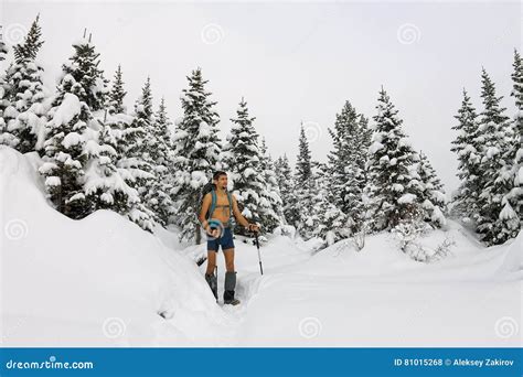 Male Tourist With A Backpack With A Naked Torso And Legs Is Among The Snowdrifts And Trees