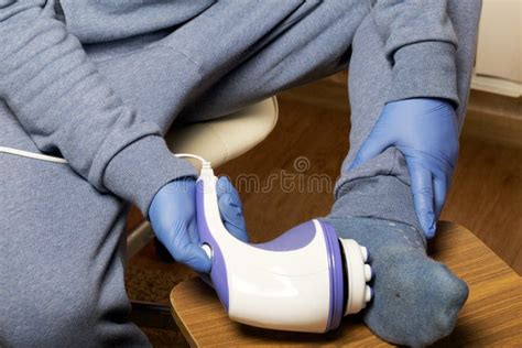 A Man Massages The Calf Muscles And Feet With An Electric Massager