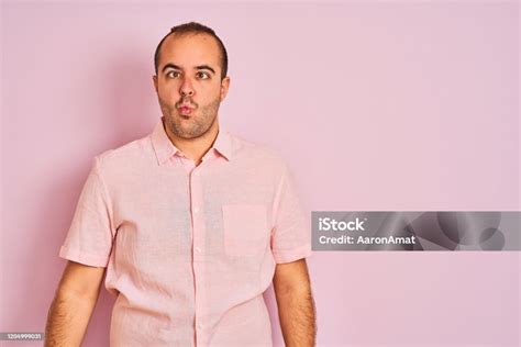고립 된 분홍색 배경 위에 서있는 우아한 셔츠를 입은 젊은 남자는 입술 미친 코믹 한 제스처로 물고기 얼굴을 만듭니다 재미있는