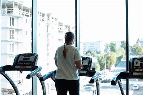 뚱뚱한 여자는 피트니스 체육관에서 디딜 방아에서 달리고 교통 교통과 도시 생활 뒷모습에서 창문을 바라 봅니다 과체중 여성은 훈련 장치에서 유산소 운동을합니다 체중 감량