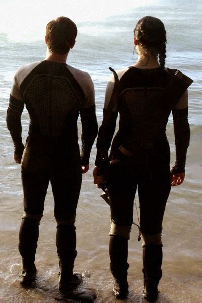 Two People In Wetsuits Standing On The Beach Looking Out At The Water