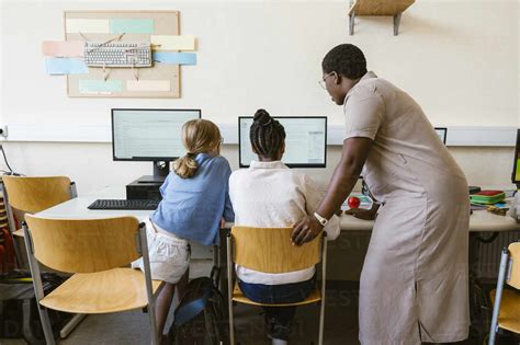 Side View Of Female Teacher Explaining Girls Using Computer While Sitting In Classroom At Babe