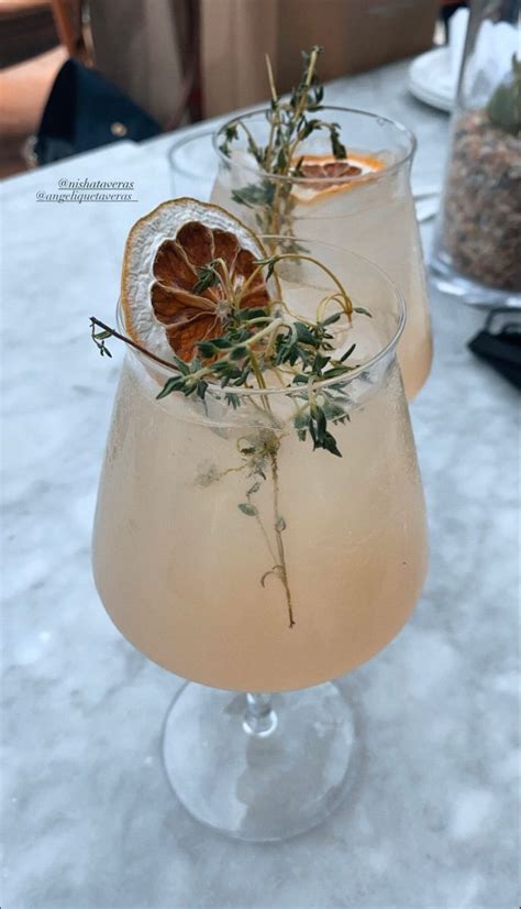 Two Glasses Filled With Drinks Sitting On Top Of A White Tablecloth
