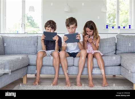 Brüder Und Schwester Auf Sofa Mit Digitalen Tablets Und Mobile