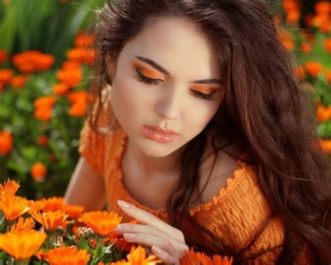 Фото Девушка в оранжевом платье касается рукой оранжевых цветов она смотрит на цветы