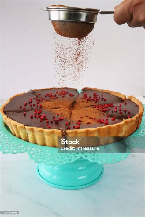 코코아 파우더의 이미지는 흰색 배경에 대한 청록색 블루 케이크 스탠드에 동결 건조 라즈베리 조각을 뿌린 바삭하고 플루티드 페이스트리 크러스트와 함께 갓 구운 얇게 썬 초콜릿