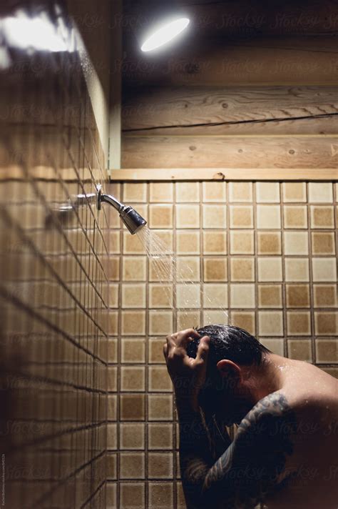 A Handsome Tattood Man Washes His Face In The Shower By Stocksy